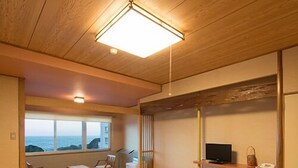 Um quarto japonês tradicional com tatames, uma mesa baixa, cadeiras, uma televisão e vista para o mar.