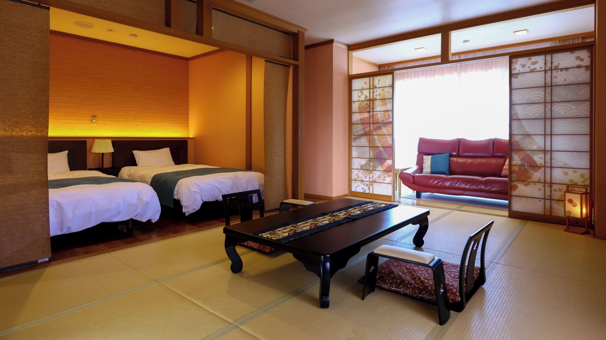 Quarto de hotel em estilo tradicional japonês, com tatames, duas camas, uma mesa baixa e um sofá vermelho.