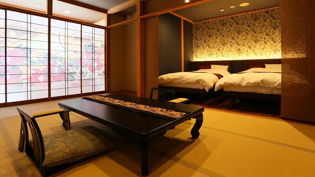 Um quarto em estilo japonês tradicional, com tatames, uma mesa baixa com almofadas e uma cama com cabeceira estampada com flores.