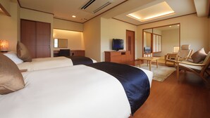 Quarto de hotel com duas camas, uma escrivaninha, televisão e área de estar com cadeiras.