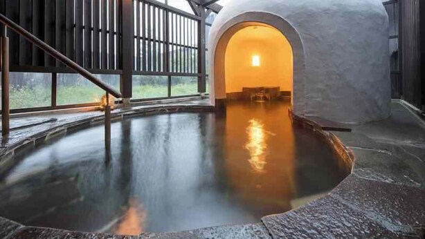 Uma sauna com arco de pedra, vigas de madeira e uma grande janela.