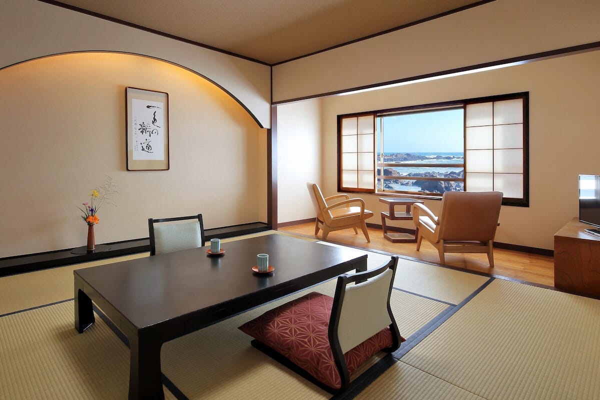 Um quarto japonês tradicional com tatames, uma mesa baixa e vista para o mar através de um shoji.