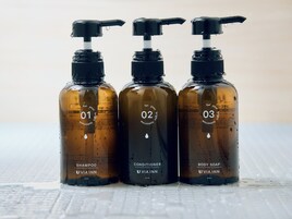 Três garrafas de produtos VIA INN sobre uma superfície com azulejos.