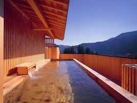 Um spa de madeira com banheira de hidromassagem, paredes de madeira e vista para as montanhas.