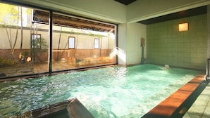 Piscina com água cristalina, rodeada por um deck de madeira e uma parede de vidro.