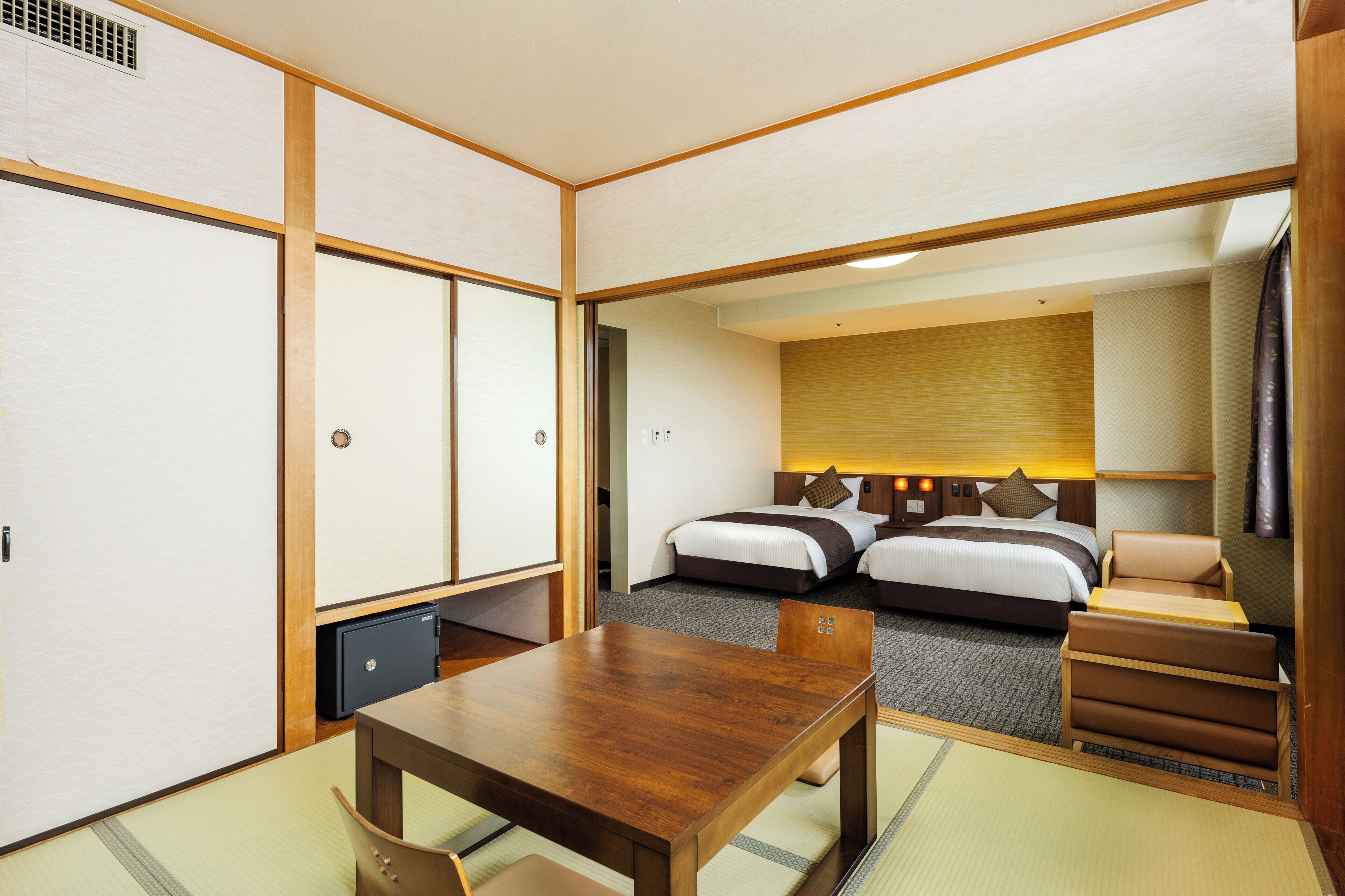 Quarto de hotel com mesa de madeira, duas camas, um sofá e uma porta tradicional japonesa de correr.