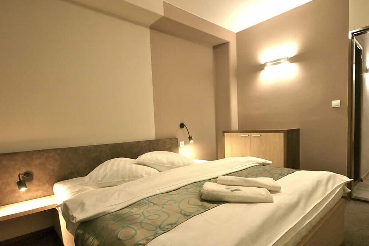 Quarto de hotel com cama, mesas de cabeceira, guarda-roupa e iluminação embutida na parede.