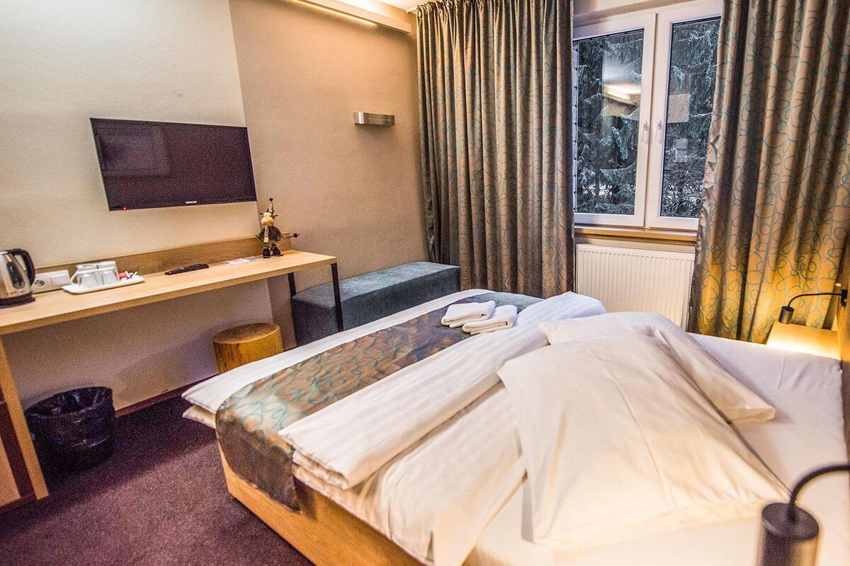 Quarto de hotel com duas camas, uma escrivaninha, uma cadeira, uma televisão e uma janela com cortinas.