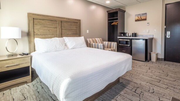 Quarto de hotel com uma cama grande, uma escrivaninha com candeeiro, micro-ondas e uma kitchenette pequena.