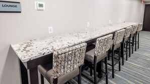 Uma sala de conferências com uma mesa comprida, cadeiras estampadas, um termostato e um letreiro com a palavra 'Lounge' na parede.