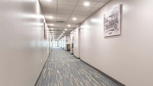 Um corredor longo e estreito com carpete estampado, paredes brancas e teto com iluminação embutida.