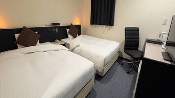 Quarto de hotel com duas camas, uma escrivaninha com computador, uma cadeira e uma pequena mesa com abajur.