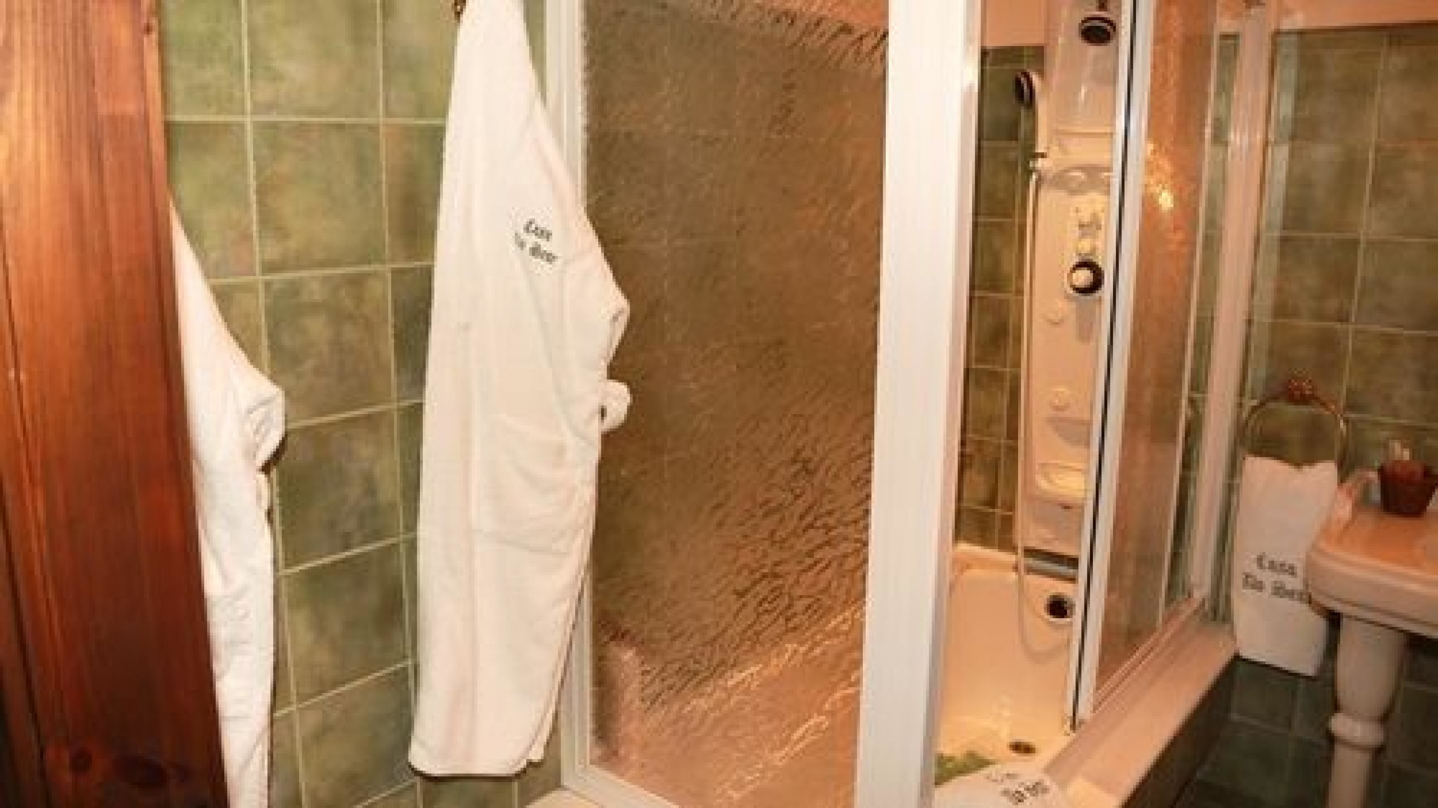 Casa de banho com cabine de duche em vidro, uma toalha branca pendurada na parede e lavatório com espelho.