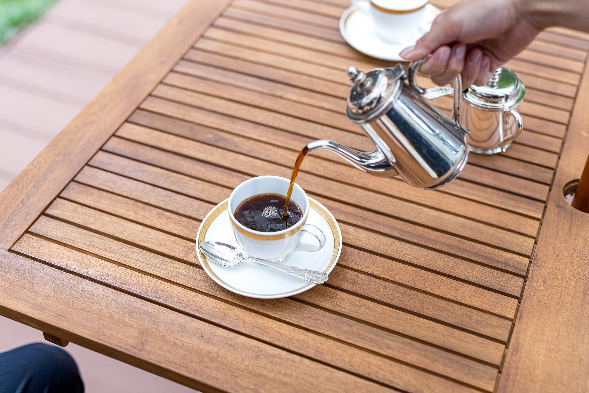 Uma mesa de madeira com uma chávena de café e uma chaleira de metal a servir.