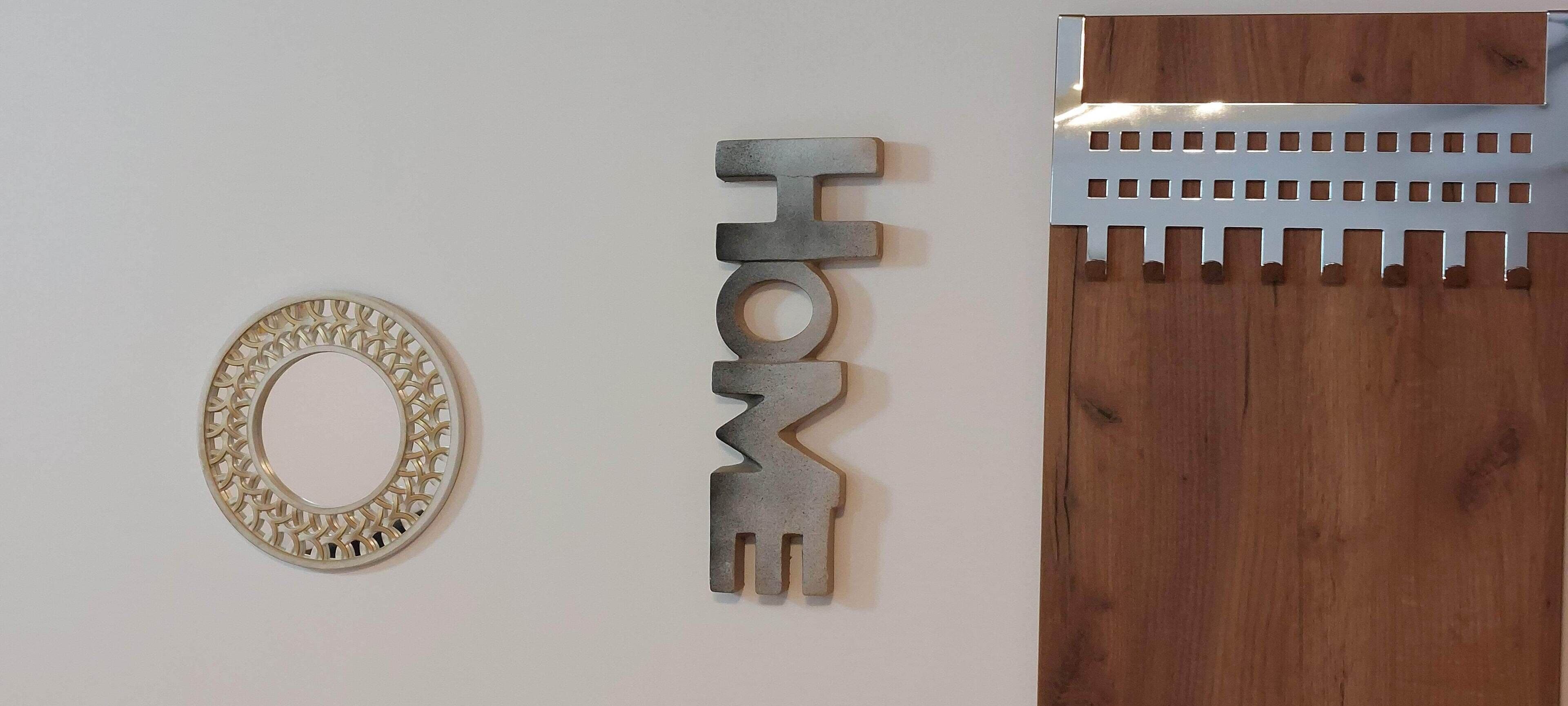 Três objetos decorativos fixados na parede: um padrão circular, um letreiro metálico com a palavra 'LOVE' e um painel de madeira com formas recortadas.