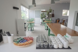 Uma área de refeições moderna com cadeiras verdes, uma mesa de madeira e diversos alimentos e suprimentos no balcão.