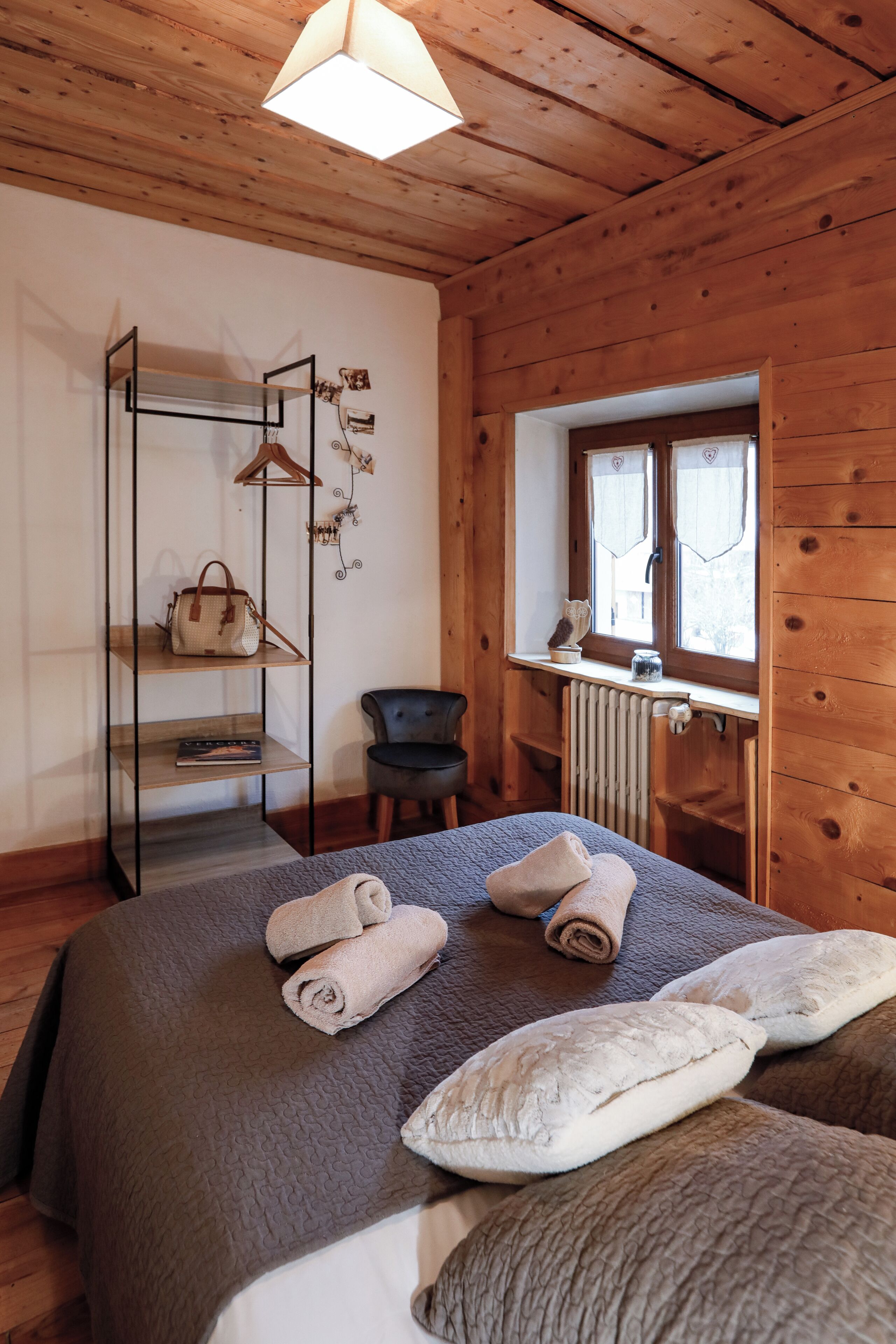 Quarto de cabana de madeira com cama, cadeira, radiador e janela com cortinas.