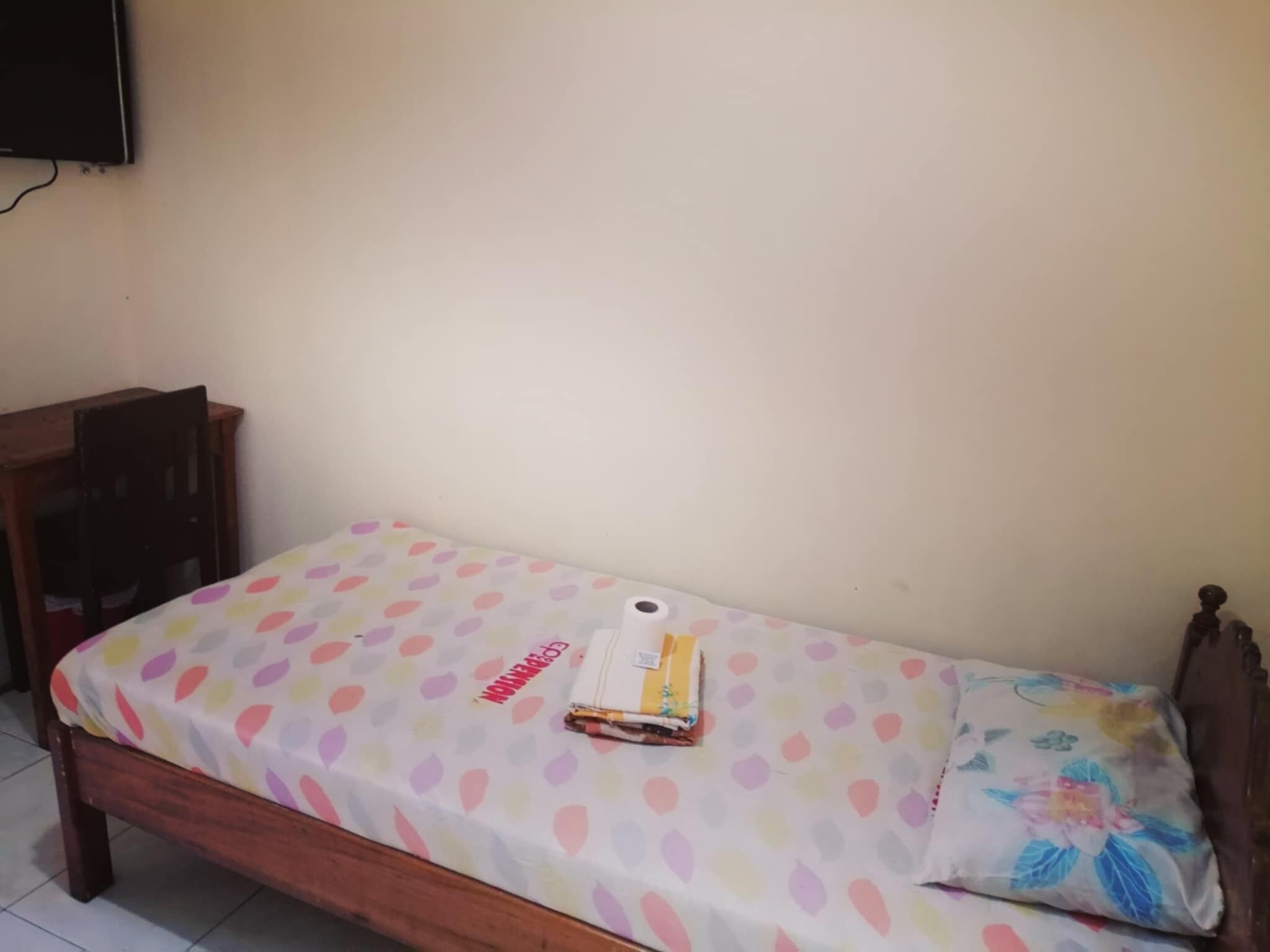 Uma cama de solteiro com edredom de bolinhas, um travesseiro estampado com flores e um cobertor dobrado sobre a cama.