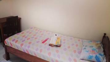 Uma cama de solteiro com edredom de bolinhas, um travesseiro estampado com flores e um cobertor dobrado sobre a cama.