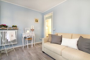 Sala de estar com sofá bege, uma cadeira branca, radiador e prateleira com plantas.