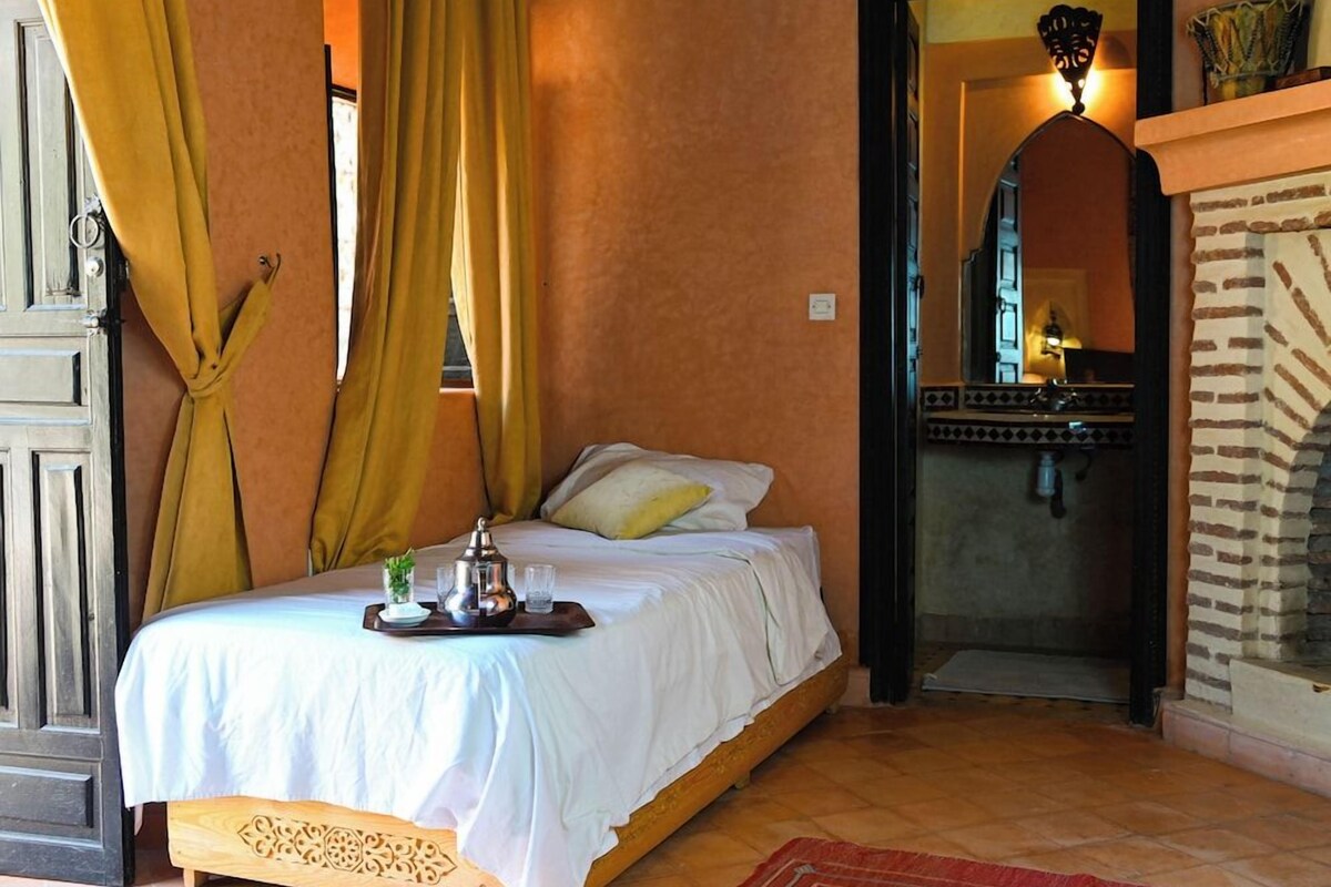 Quarto com cama, mesa de cabeceira, espelho e lareira.
