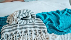 Uma cama com um cobertor listrado e um travesseiro de macramé, um cobertor azul-turquesa e uma pessoa lendo um livro.