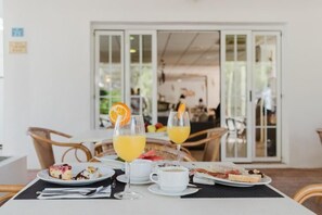 Mesa de jantar com pratos de comida, copos de suco de laranja e uma xícara branca, possivelmente em um restaurante ou café.