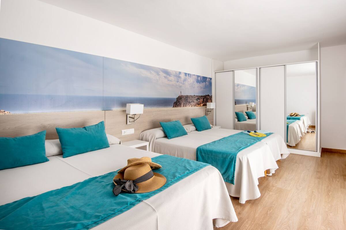 Quarto de hotel com duas camas, uma janela grande com vista para a costa e uma porta deslizante que dá para uma varanda.