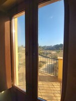 Quarto com grandes janelas que oferecem vista para área pavimentada e edifícios ao longe.