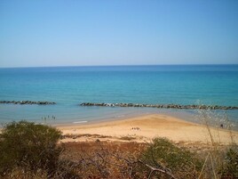 Uma praia com águas azul-claras, areal arenoso e paredões rochosos.