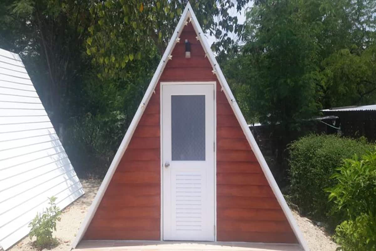 Um edifício em formato triangular com uma porta branca e uma pequena janela.