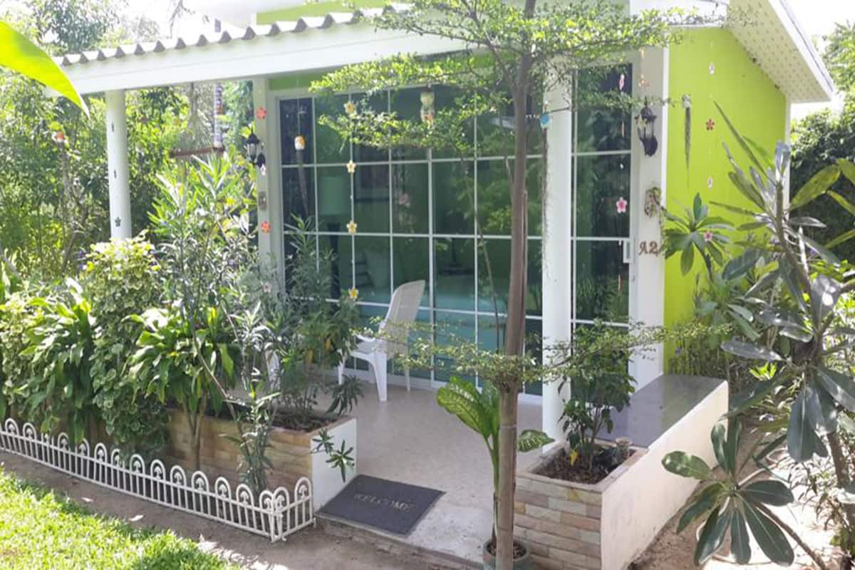 Um edifício moderno com fachada de vidro, entrada coberta com guarda-corrimão branco e diversos vasos de plantas.