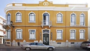 Um edifício amarelo com porta preta, várias janelas e uma varanda.