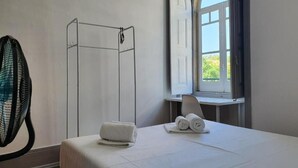 Quarto de hotel com cama, janela com cortinas, cadeira e porta-toalhas.