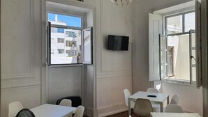 Quarto com televisão na parede, um candelabro e uma janela com a porta aberta.