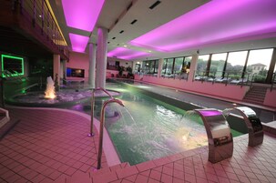 Piscina interior com fonte de água, guarda-corpo de vidro e vista para o exterior através de amplas janelas.