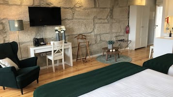 Quarto moderno com parede de pedra, televisão de tela plana, escrivaninha com cadeira, mesinha com objetos decorativos, guarda-roupa e cama com roupa de cama verde.