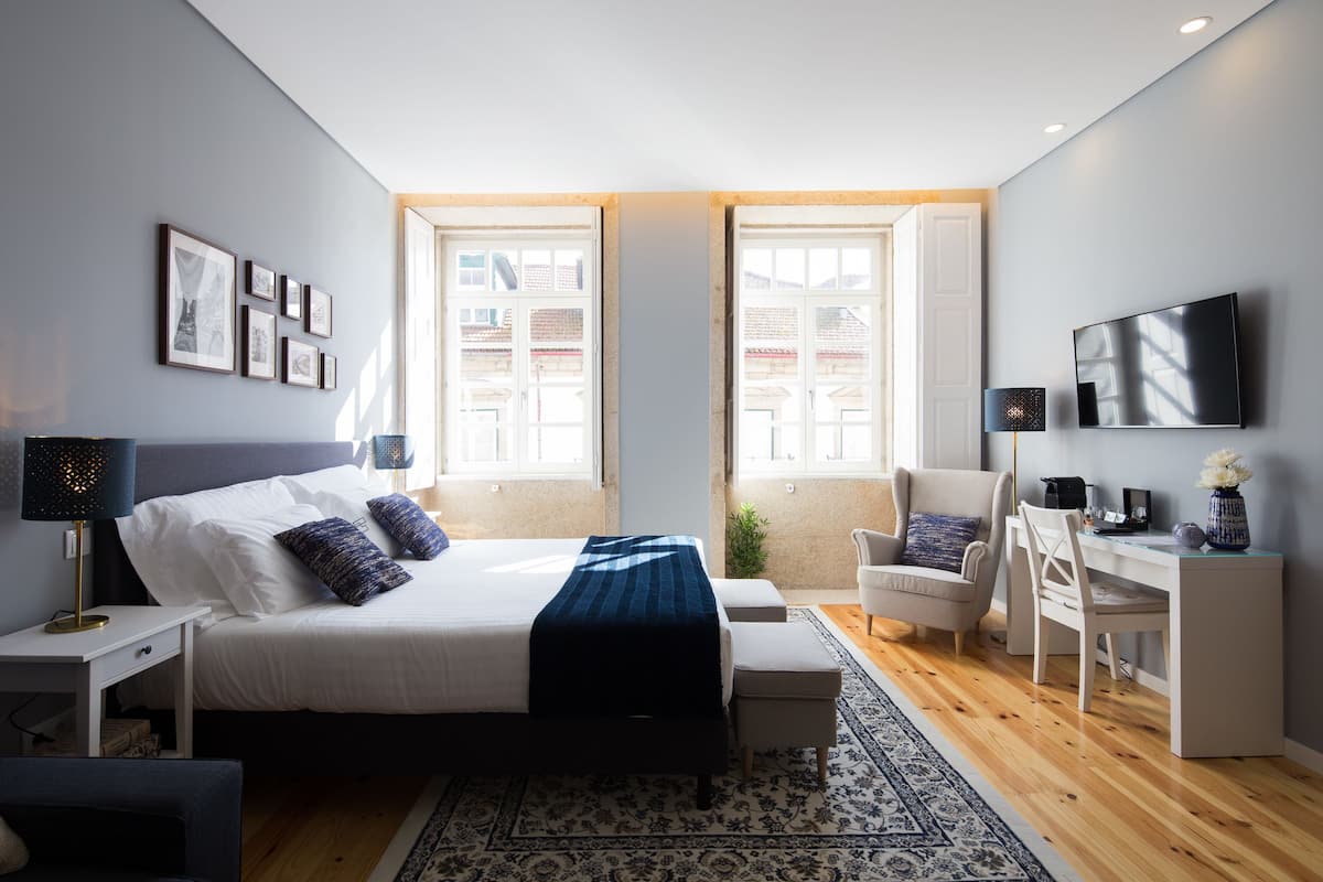 Quarto moderno com cama, mesa de cabeceira, escrivaninha, cadeira e televisão.