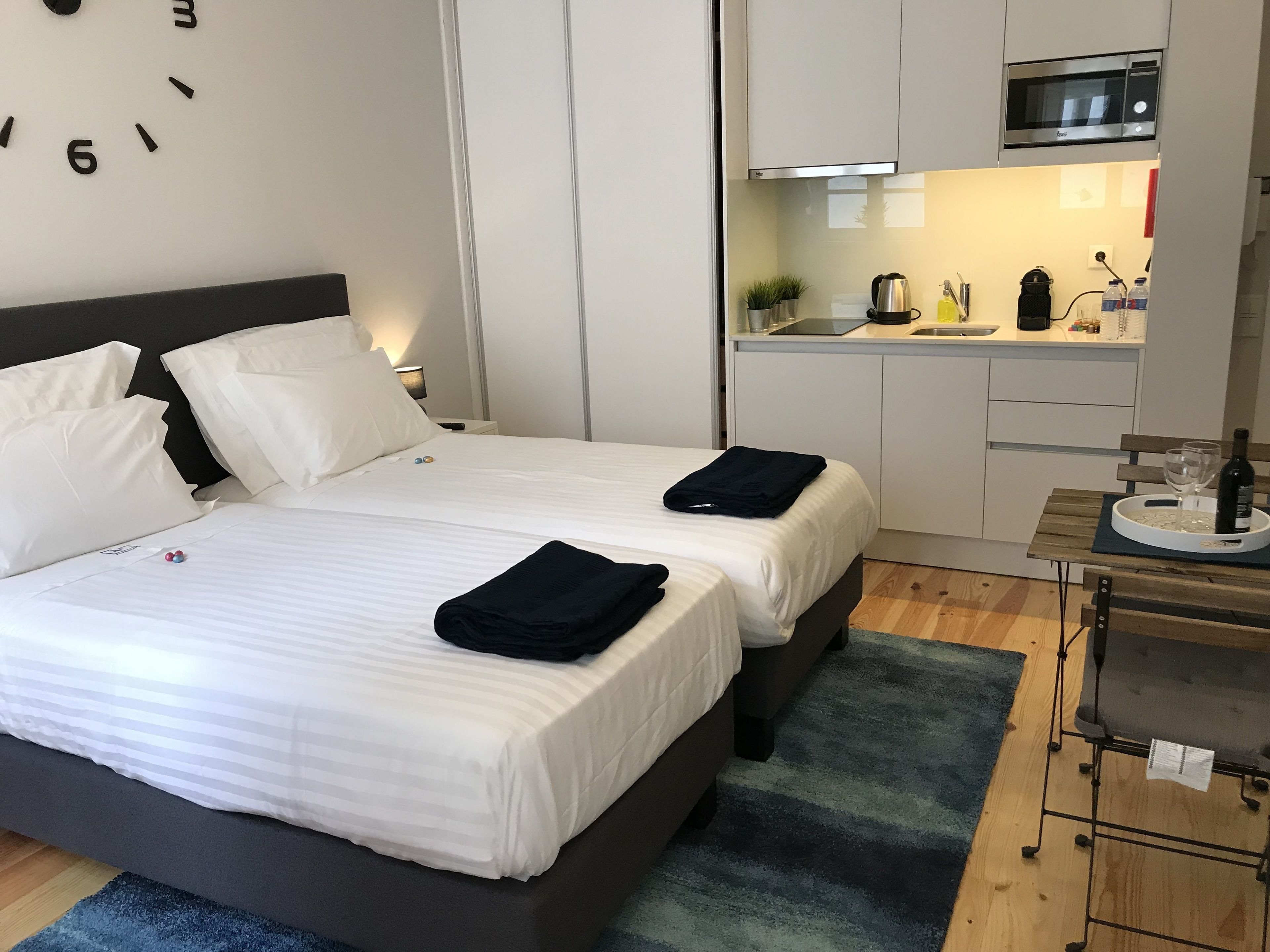 Quarto de hotel com duas camas, micro-ondas, pia e uma pequena mesa com garrafa e copos.