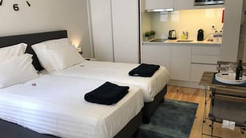 Quarto de hotel com duas camas, micro-ondas, pia e uma pequena mesa com garrafa e copos.