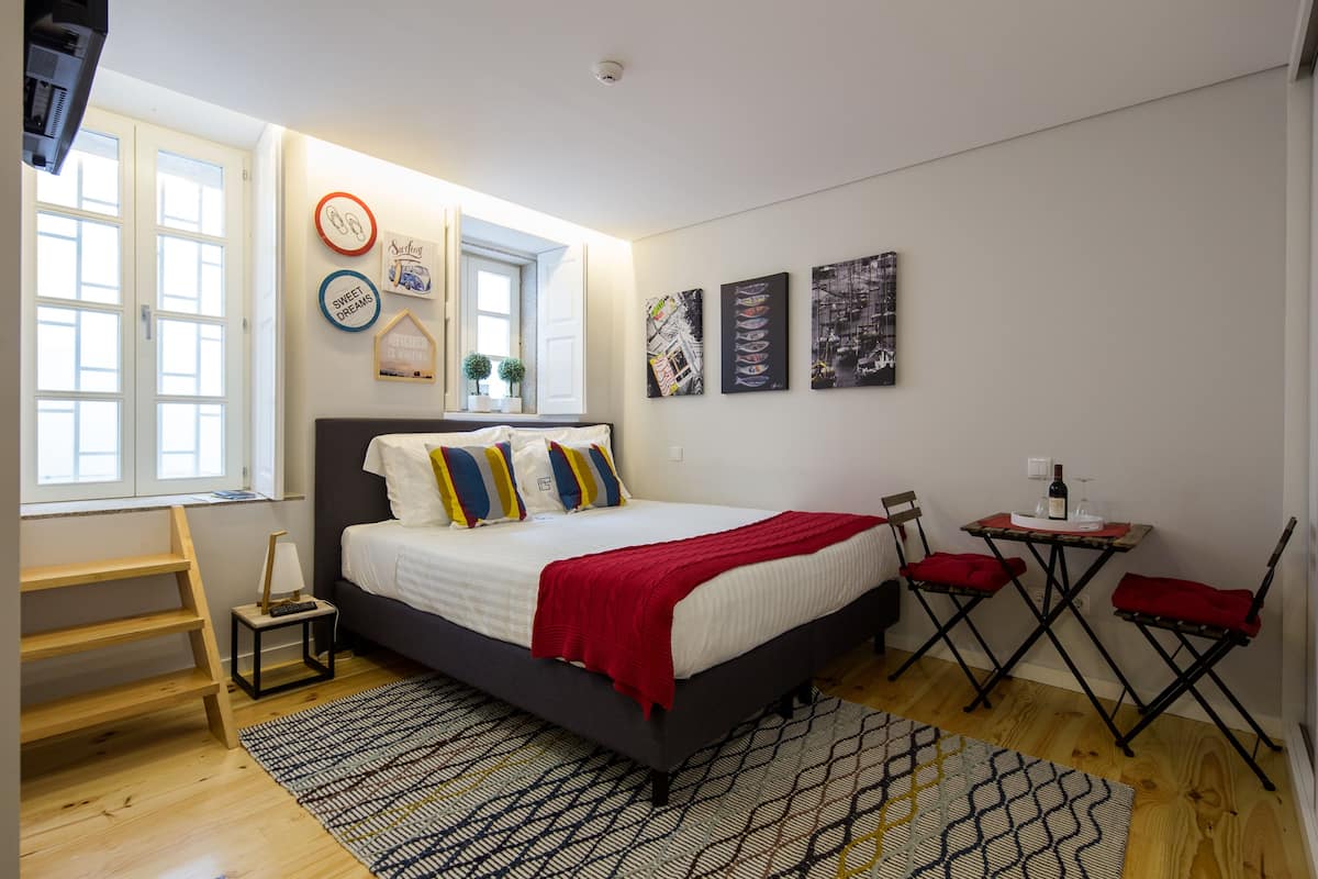 Quarto com cama, janela, escrivaninha e duas cadeiras.