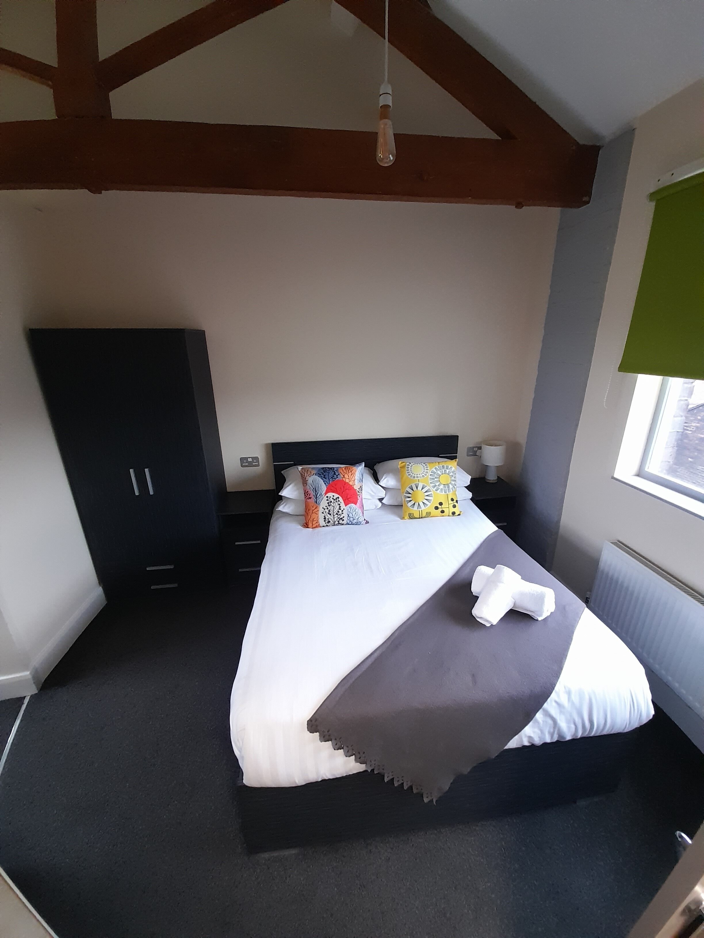 Quarto com cama, guarda-roupa, mesa de cabeceira, luminária e janela com vista.