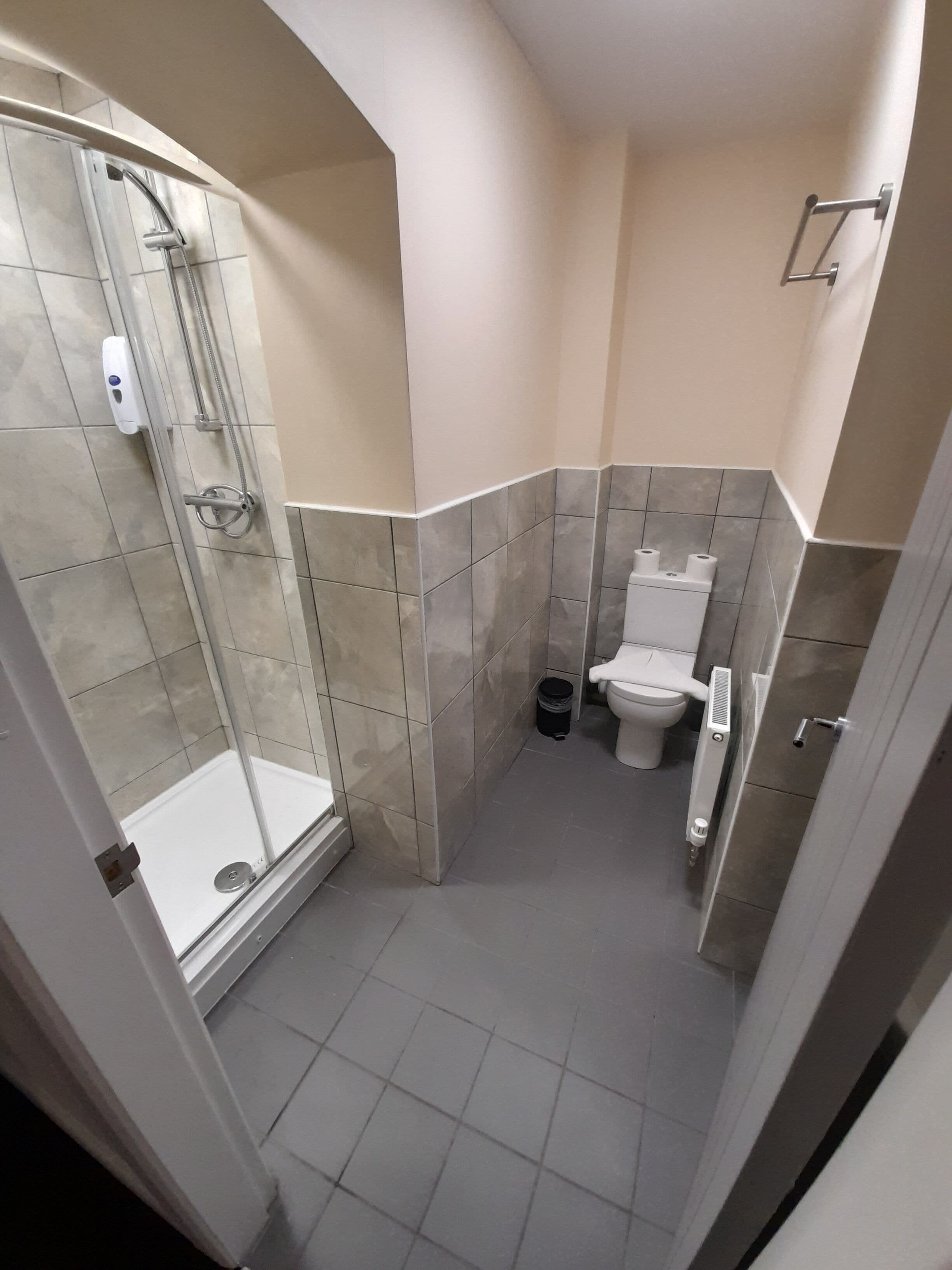 Casa de banho compacta com chuveiro separado por vidro, sanita e um lixo.