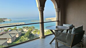Varanda com mesa e cadeira, vista para a costa com palmeiras e uma praia.