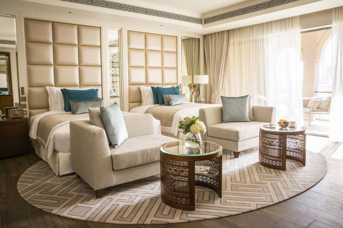 Quarto de hotel com uma cama grande, dois sofás, uma mesa de centro redonda e um tapete estampado.