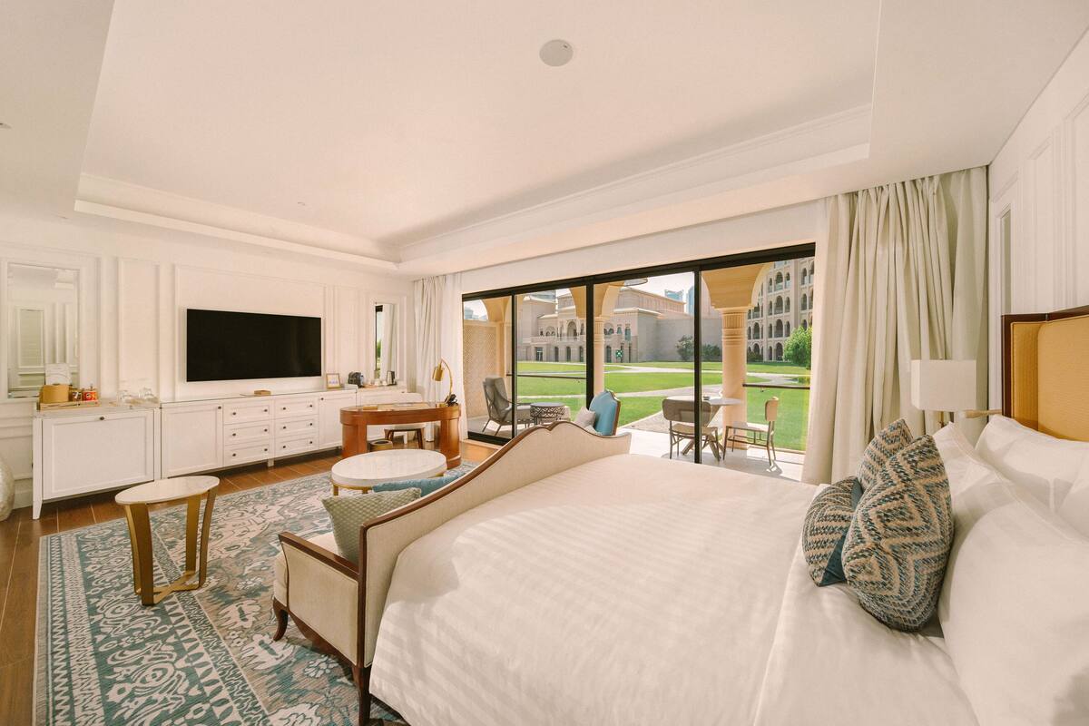 Quarto de hotel espaçoso com uma cama grande, televisão de tela plana, área de refeições e varanda com vista para um edifício.