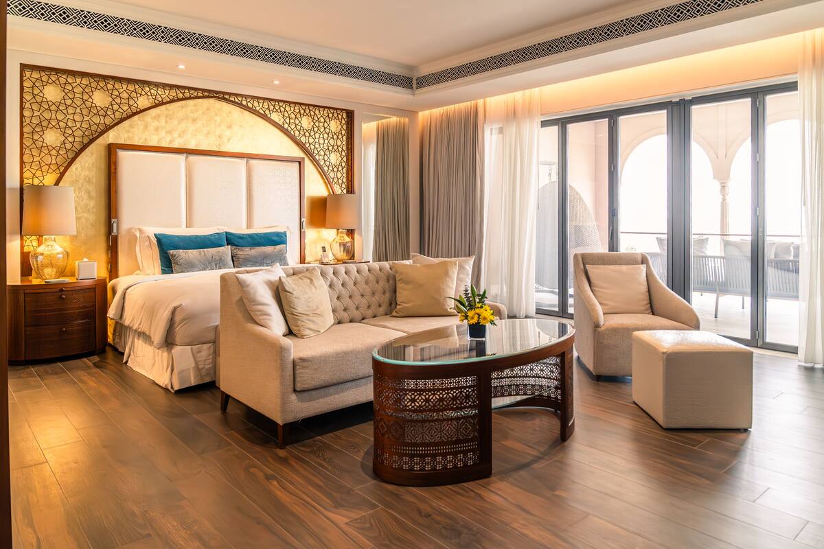 Um quarto de hotel espaçoso com uma cama grande, um sofá, uma poltrona e uma mesa de centro de vidro.
