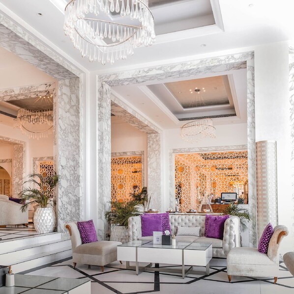 Uma sala de estar luxuosa com paredes de mármore, teto alto e lustres elegantes.