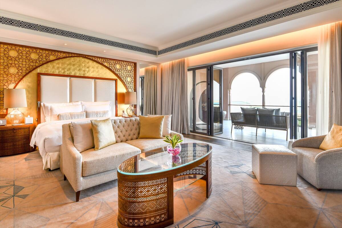 Quarto de hotel espaçoso com uma cama grande, um sofá, uma mesa de centro de vidro e varanda com vista.