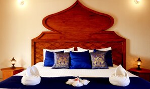 Uma cama com cabeceira de madeira, almofadas azuis com padrão, roupa de cama branca e duas mesas de cabeceira com abajures.